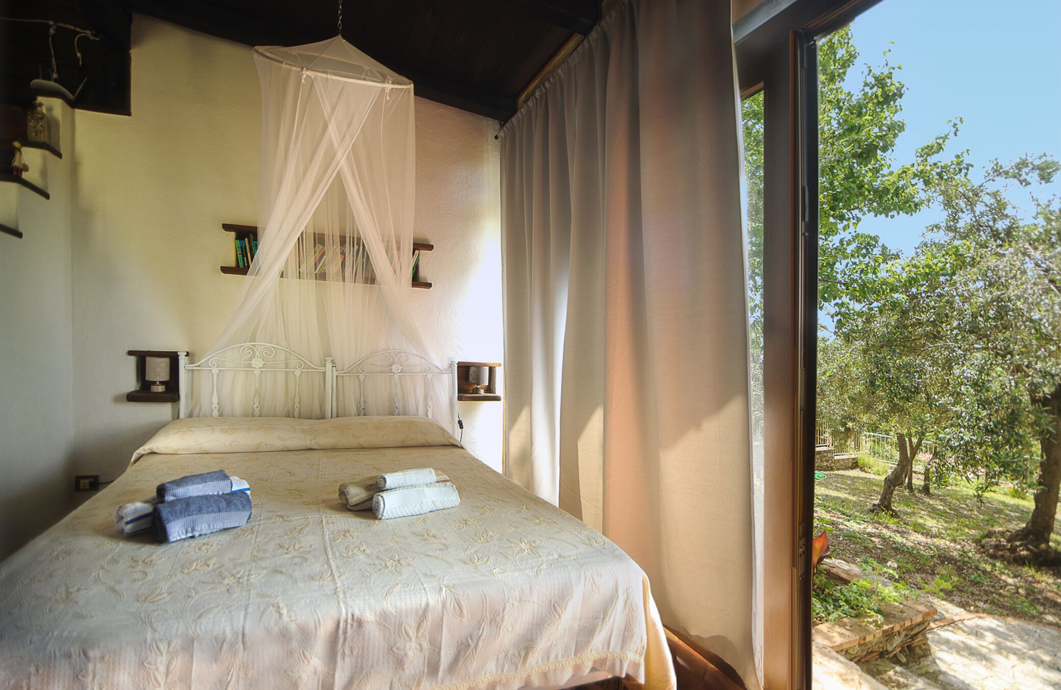 Quarto com cama de dossel, vista para o exterior e mesa de cabeceira com abajur.