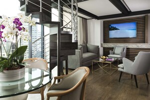 Uma sala de estar moderna com uma mesa de vidro, cadeiras de vime, um sofá cinza e uma televisão de tela plana presa à parede.
