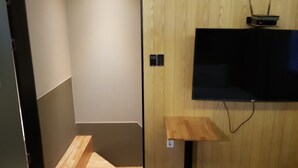 Quarto moderno com televisão de tela plana fixada numa parede de madeira, uma pequena mesa de madeira e uma escada que leva a outro andar.