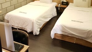 Quarto de hotel com duas camas de solteiro, uma escrivaninha com computador e uma cadeira.