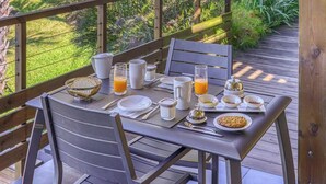 Um deck de madeira com uma mesa posta para o café da manhã, com vista para uma piscina e vegetação exuberante.