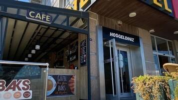 Um edifício com um café e uma padaria, um cão deitado no pavimento, e uma placa de hotel.