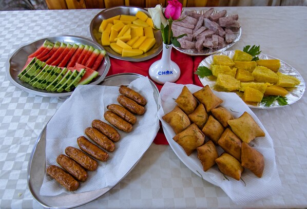 Uma mesa com diversos alimentos, incluindo melancia em fatias, manga, salsichas e doces fritos.