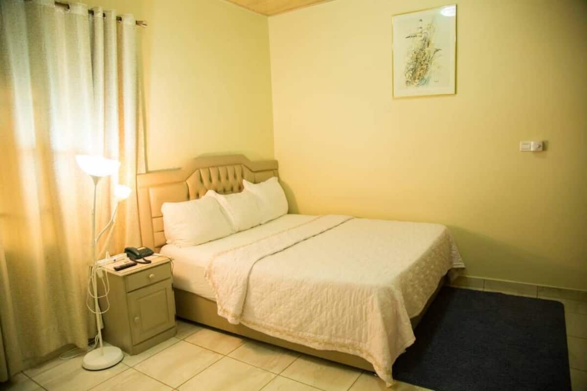 Quarto com cama, mesa de cabeceira, luminária e um quadro na parede.