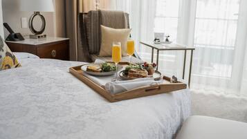 Cama arrumada com bandeja de café da manhã, incluindo torradas, salada e suco de laranja.