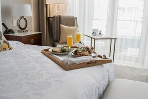 Cama arrumada com bandeja de café da manhã, incluindo torradas, salada e suco de laranja.