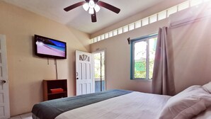 Um quarto com cama, televisão na parede, porta e janela com cortinas.