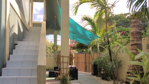 Escadaria que leva a uma área coberta com um toldo verde, cercada por plantas em vasos e uma palmeira.