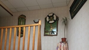 Uma escadaria com corrimão de madeira, um vaso de planta e arte decorativa na parede, incluindo um farol e uma pintura de paisagem.
