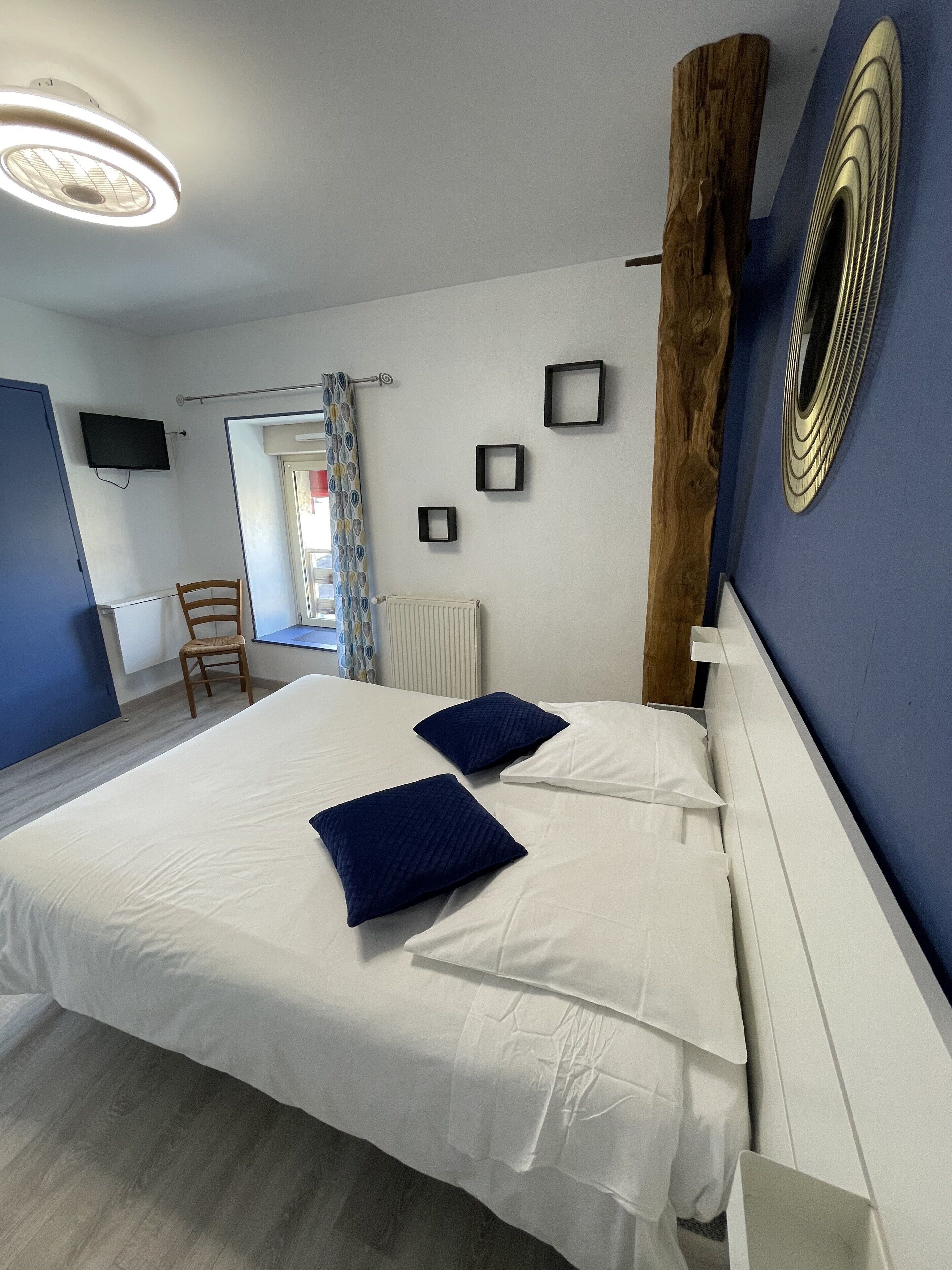 Quarto com cama grande, cabeceira de madeira, TV montada e janela com cortinas.