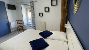 Quarto com cama grande, cabeceira de madeira, TV montada e janela com cortinas.