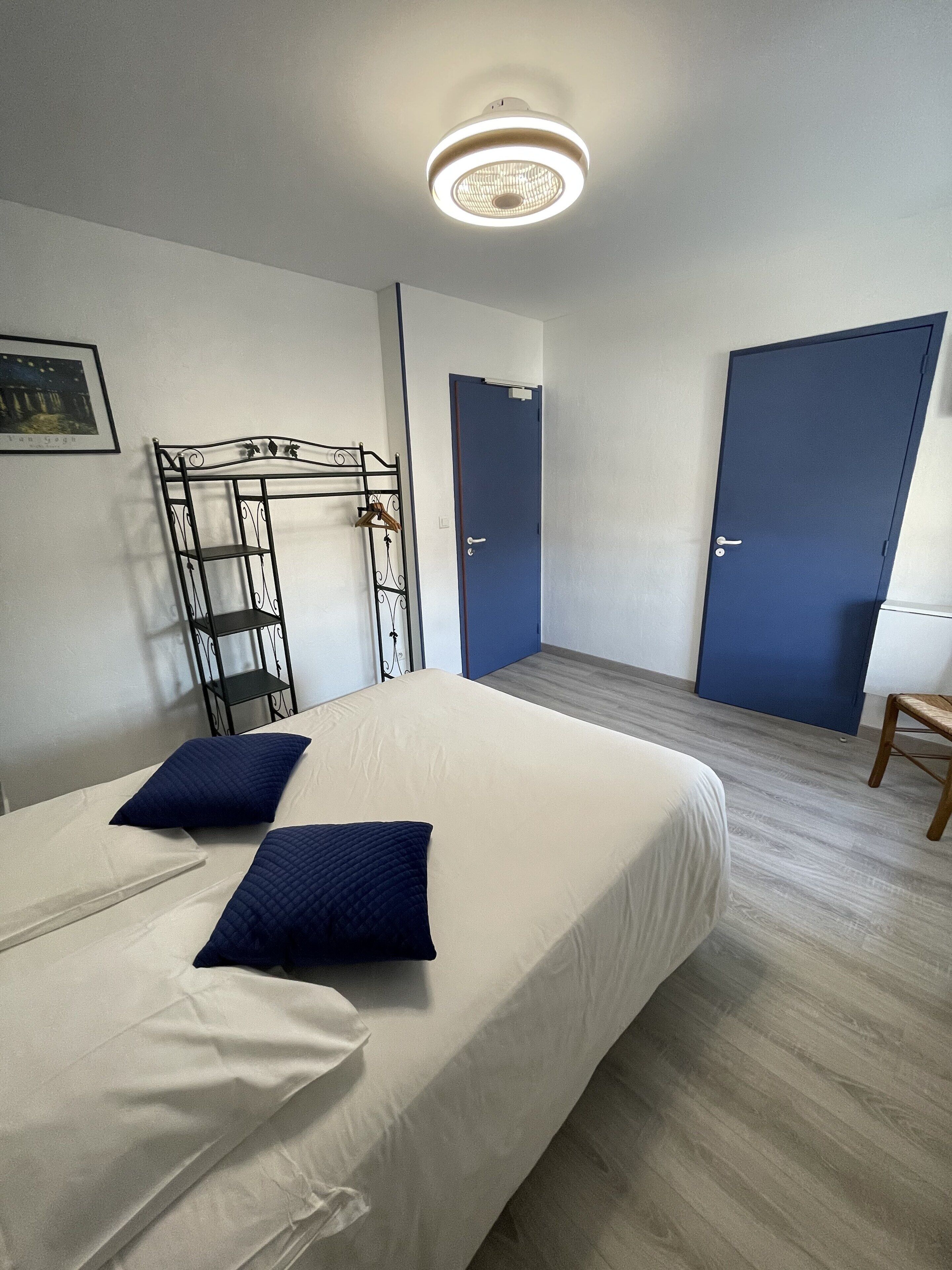 Quarto com cama, duas almofadas, um suporte de metal, duas portas e uma luminária no teto.