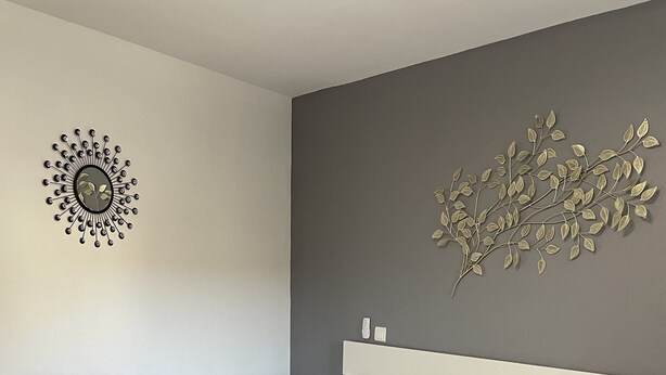 Quarto moderno com uma cama grande, cabeceira branca e um detalhe decorativo na parede.