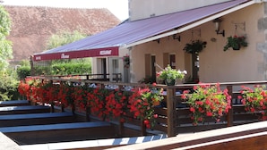 Restaurante com mesas ao ar livre, toldo vermelho e cestos de flores pendurados.