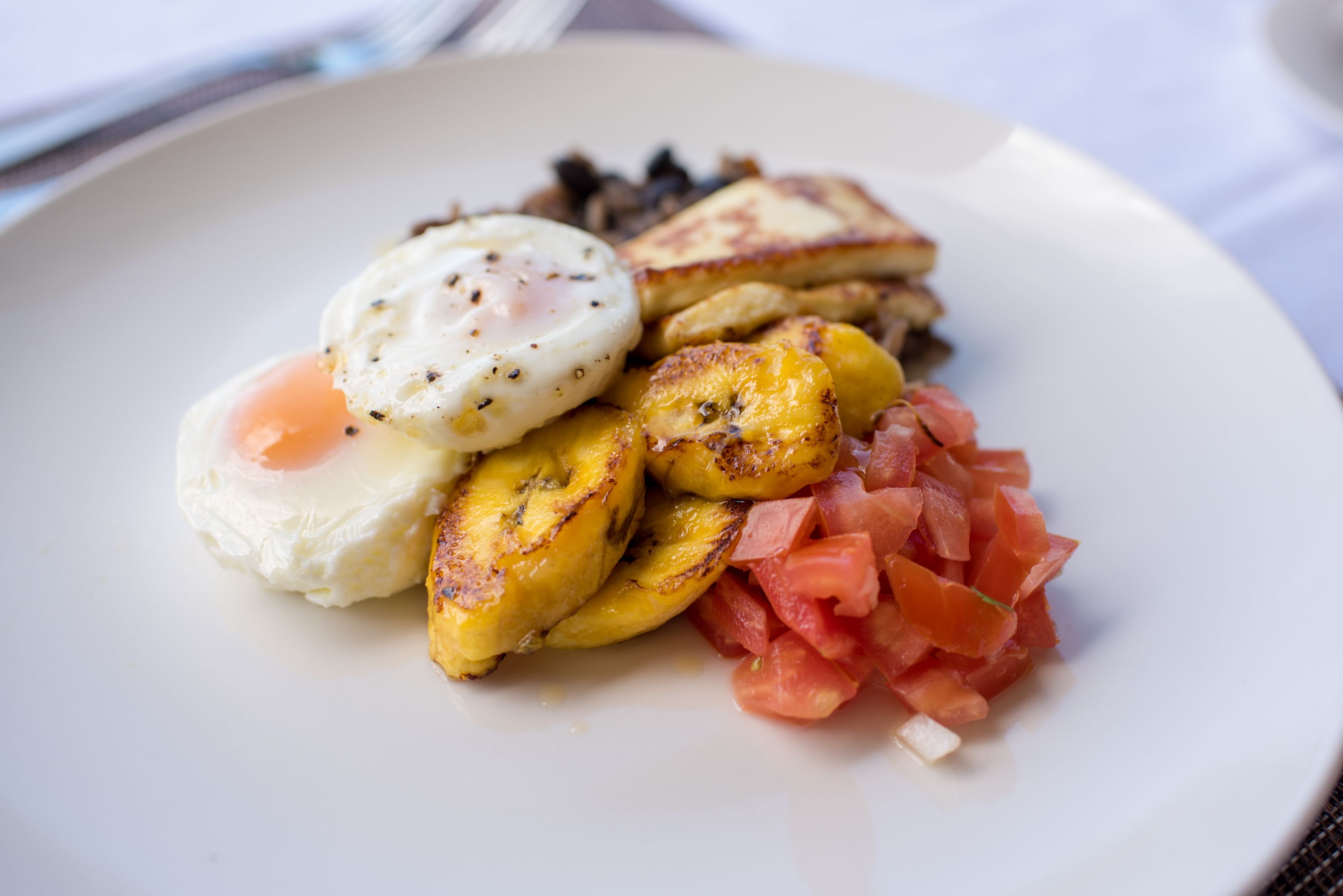 Um prato com ovo frito, bananas grelhadas e tomate picado.