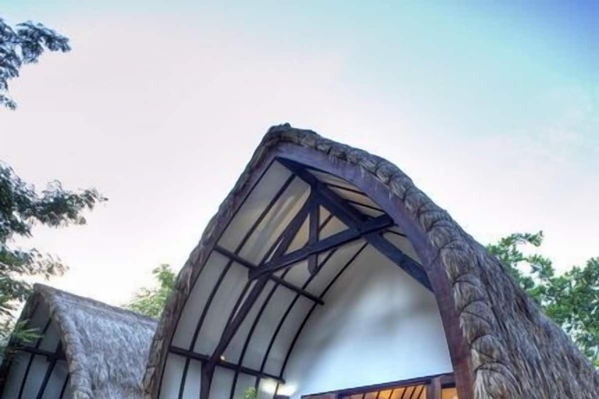 Uma cabana com telhado de palha e varanda de madeira, com degraus que levam à entrada.