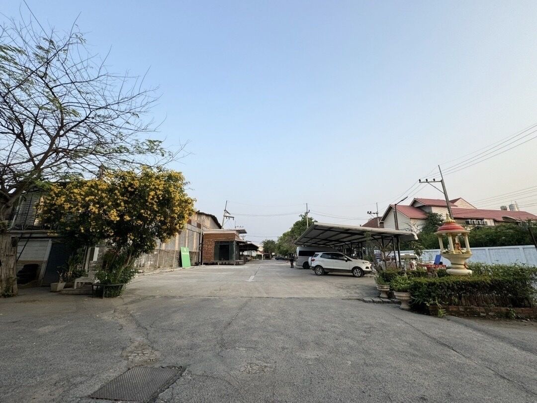 Rua residencial com casas, um carro estacionado e uma área coberta com uma fonte.
