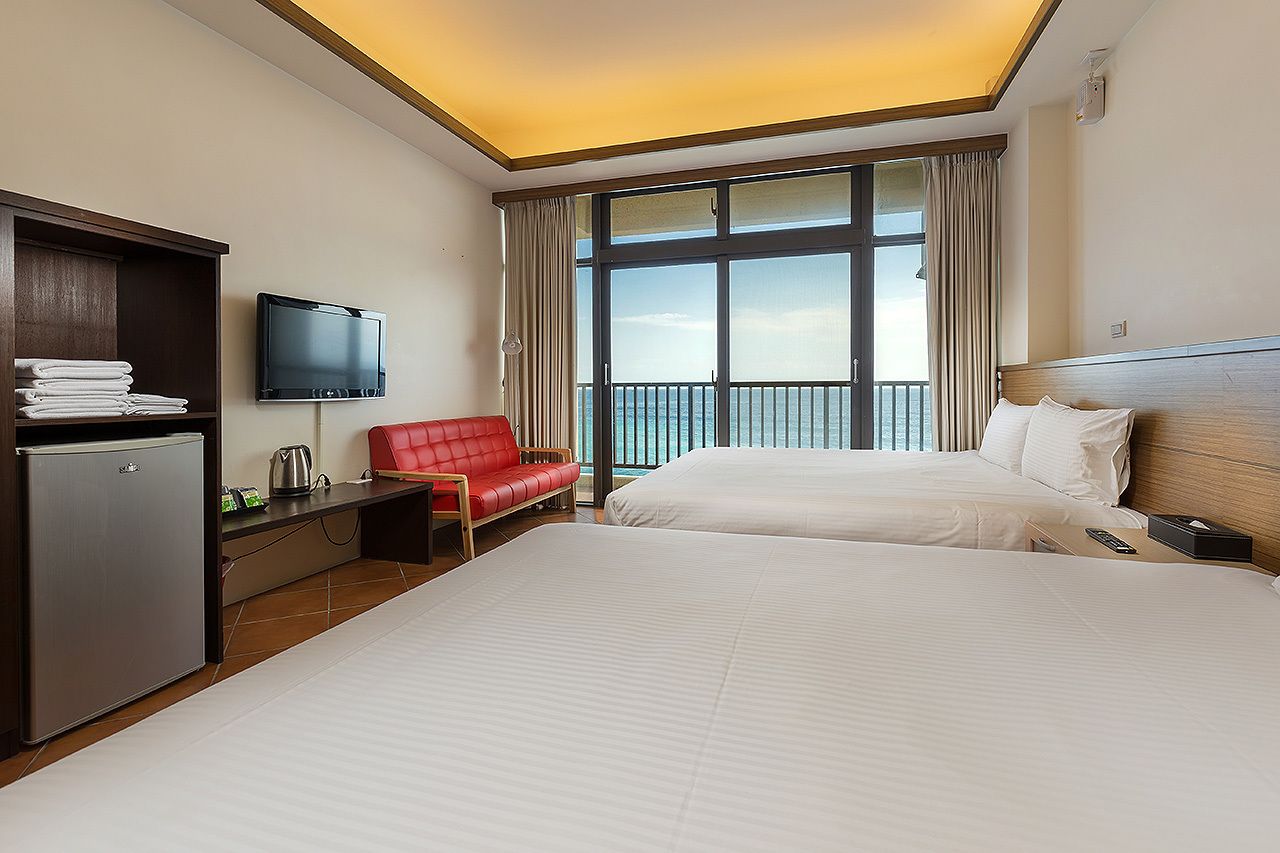 Quarto de hotel com duas camas, televisão, sofá vermelho, varanda com vista e minibar.