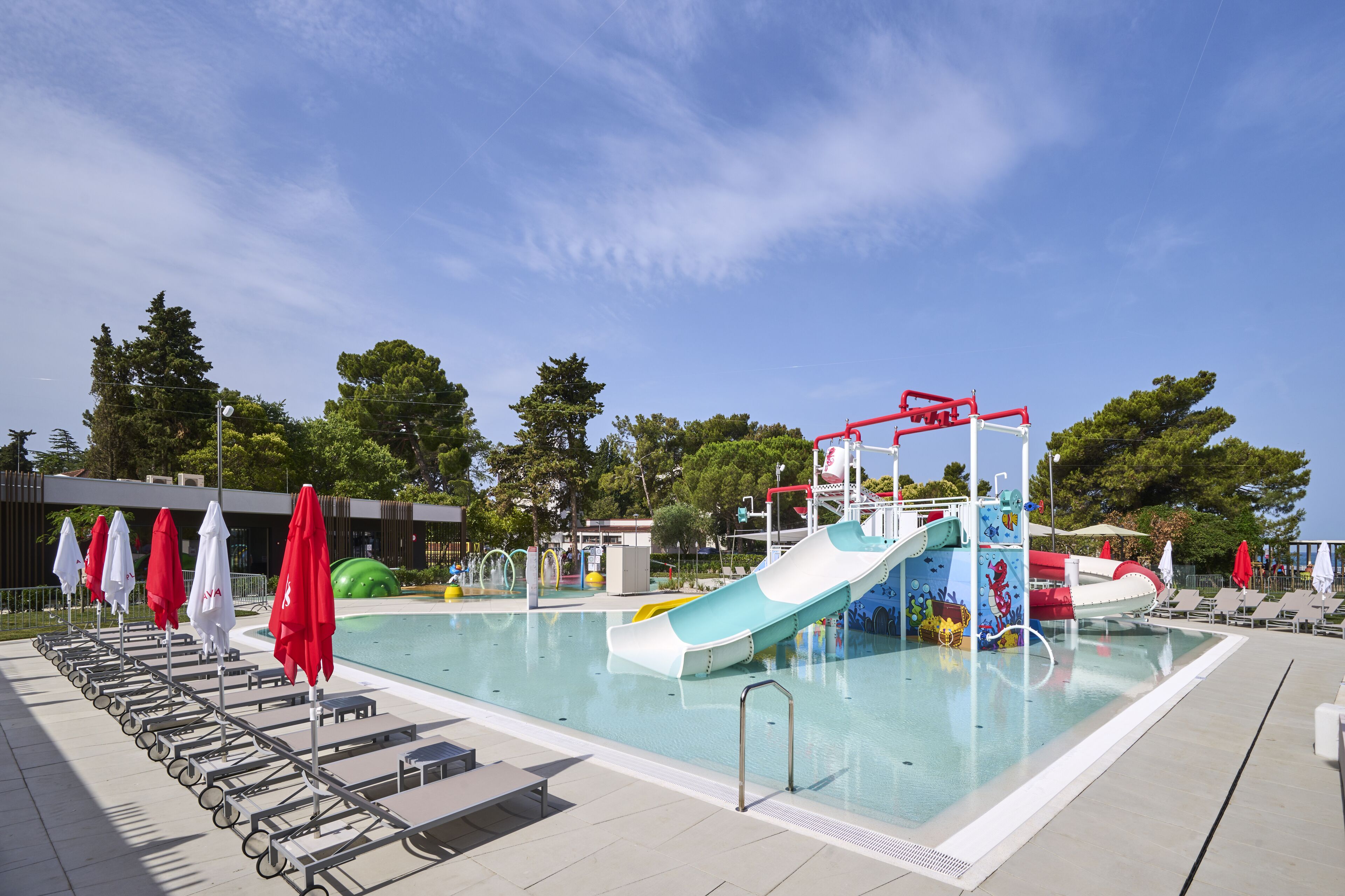Uma piscina com escorregador, espreguiçadeiras e guarda-sóis.