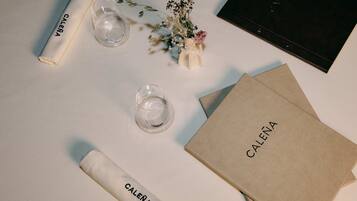 Uma mesa com um objeto enrolado identificado como 'CALENA', um vaso com flores e uma pasta preta.