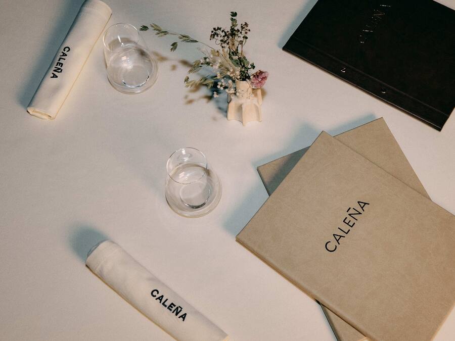 Uma mesa com um objeto enrolado identificado como 'CALENA', um vaso com flores e uma pasta preta.