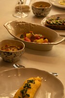 Uma mesa de jantar com diversos pratos, incluindo uma saladeira de salada de frutas, uma tigela de sopa e um prato com um omelete enrolado.