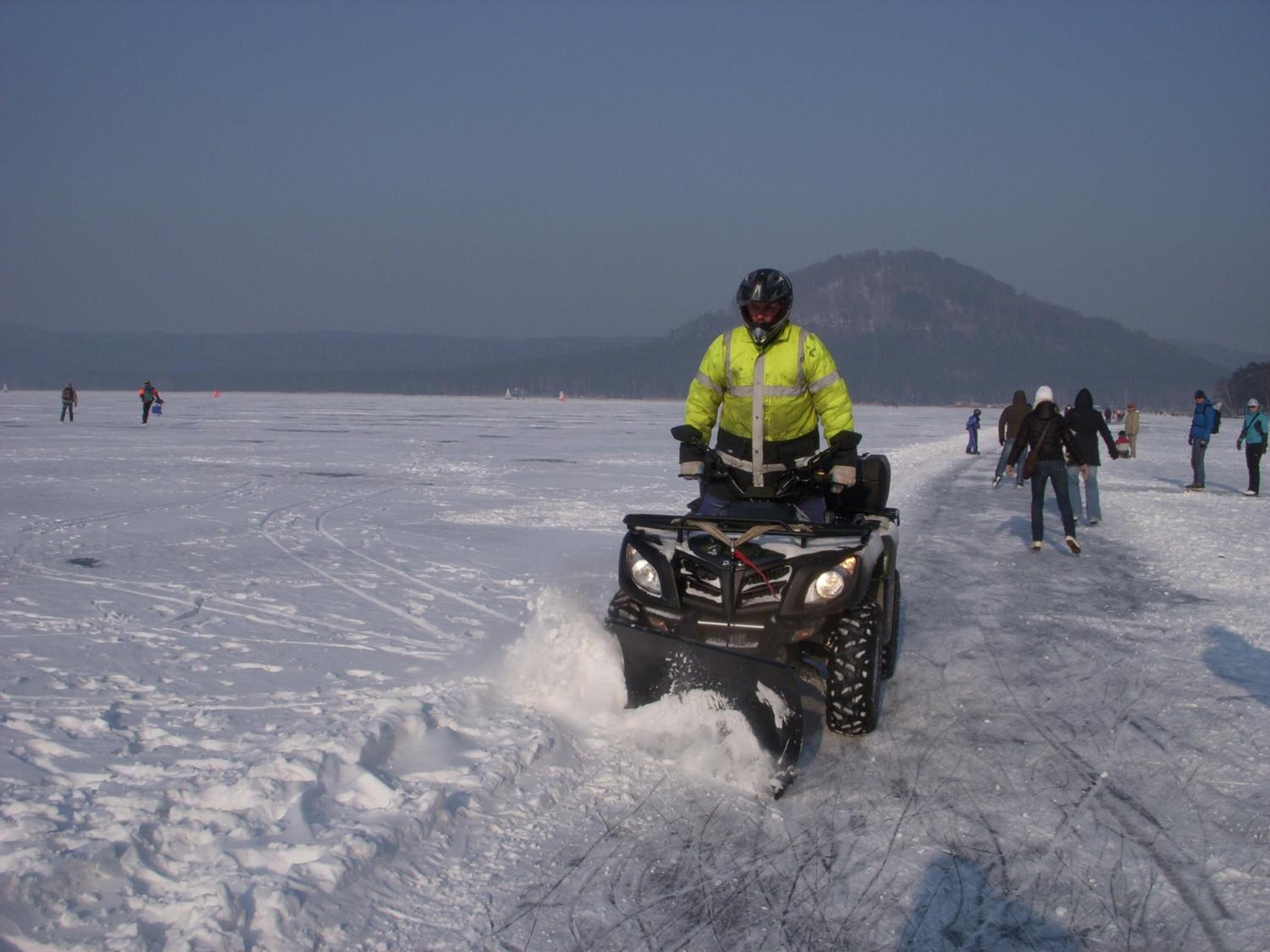 Uma pessoa andando em um snowmobile sobre um lago congelado, com montanhas ao fundo.