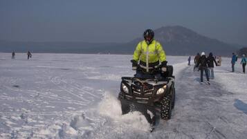 Uma pessoa andando em um snowmobile sobre um lago congelado, com montanhas ao fundo.