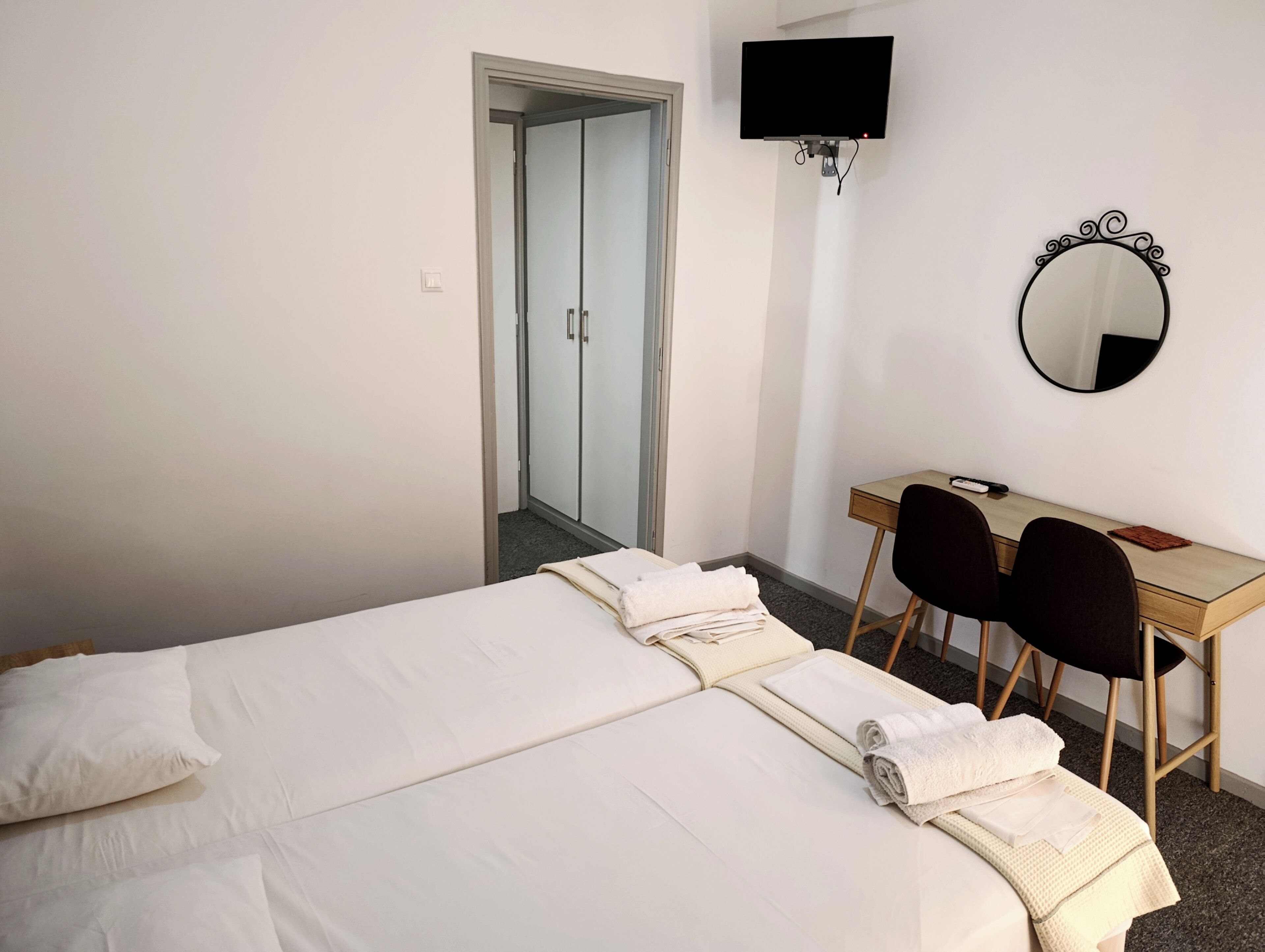 Quarto de hotel com uma cama, uma escrivaninha com cadeira, uma televisão e um espelho.