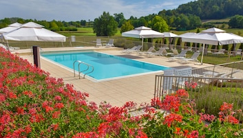 Piscina com espreguiçadeiras e guarda-sóis, cercada por uma grade e flores vermelhas.