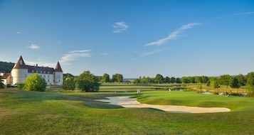 Um campo de golfe com um castelo ao fundo, bunkers de areia e um lago.