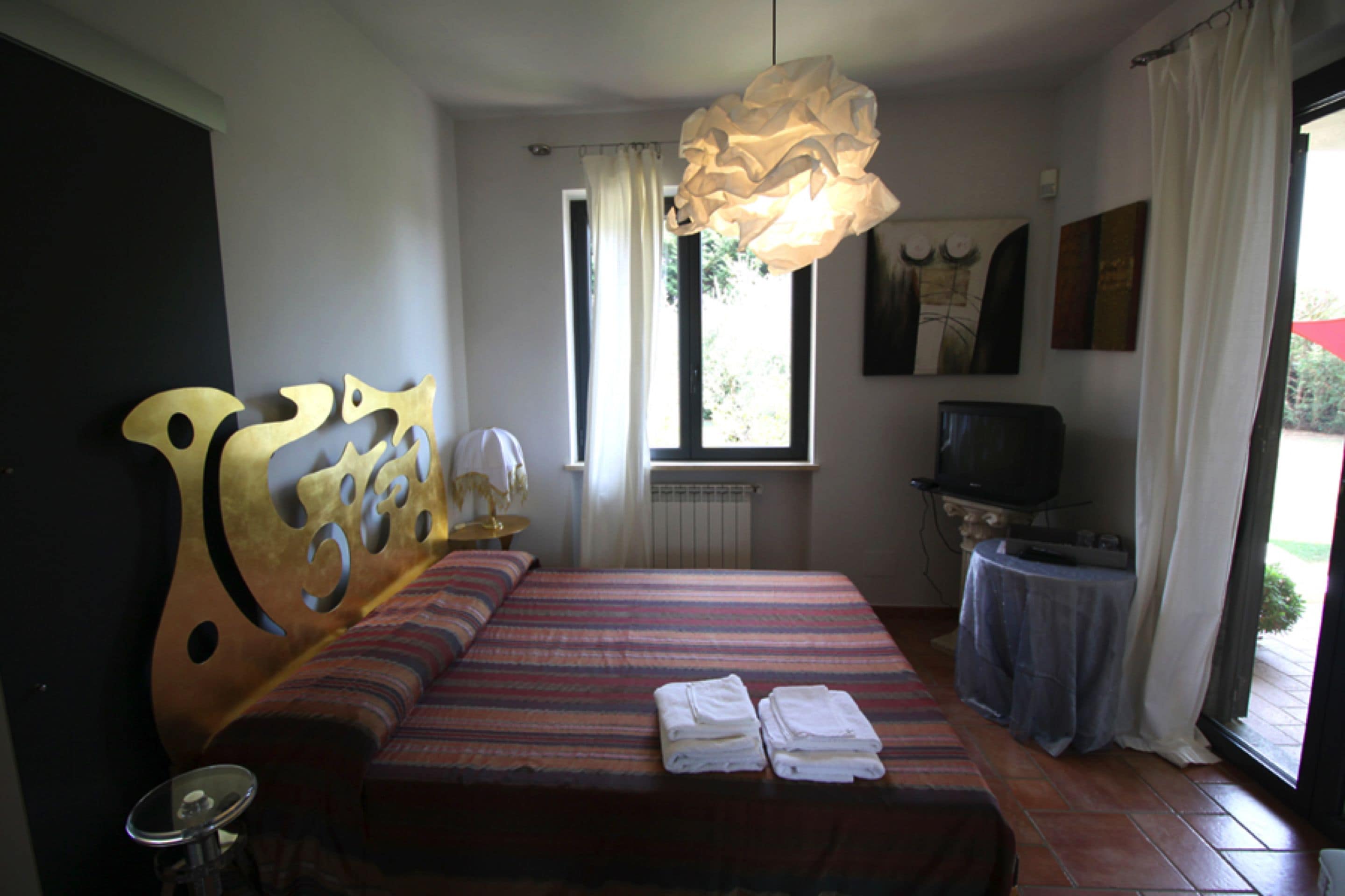 Quarto de hotel com cama, televisão, janela com cortinas e um objeto decorativo na parede.