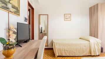 Quarto de hotel com cama, televisão, escrivaninha com um vaso de flores e espelho.