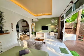 Uma sala de estar moderna com sofá, mesa de centro, televisão e uma porta de vidro deslizante que dá para uma varanda.
