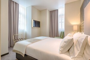 Quarto de hotel com uma cama grande, televisão de tela plana na parede e mesa de cabeceira com abajur.