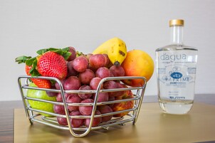 Uma cesta de frutas com morangos, uvas e uma manga, e uma garrafa de d'Agua sobre uma mesa.