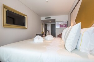 Quarto de hotel com uma cama grande, uma televisão de tela plana na parede, um espelho e um quadro emoldurado na parede.