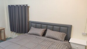 Quarto com cama, mesa de cabeceira, escrivaninha e janela com cortinas.