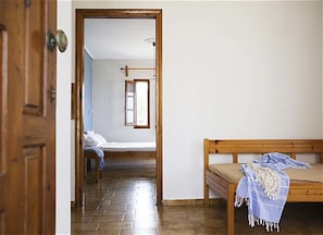 Um quarto com porta de madeira, uma cama com manta azul e um banco de madeira.