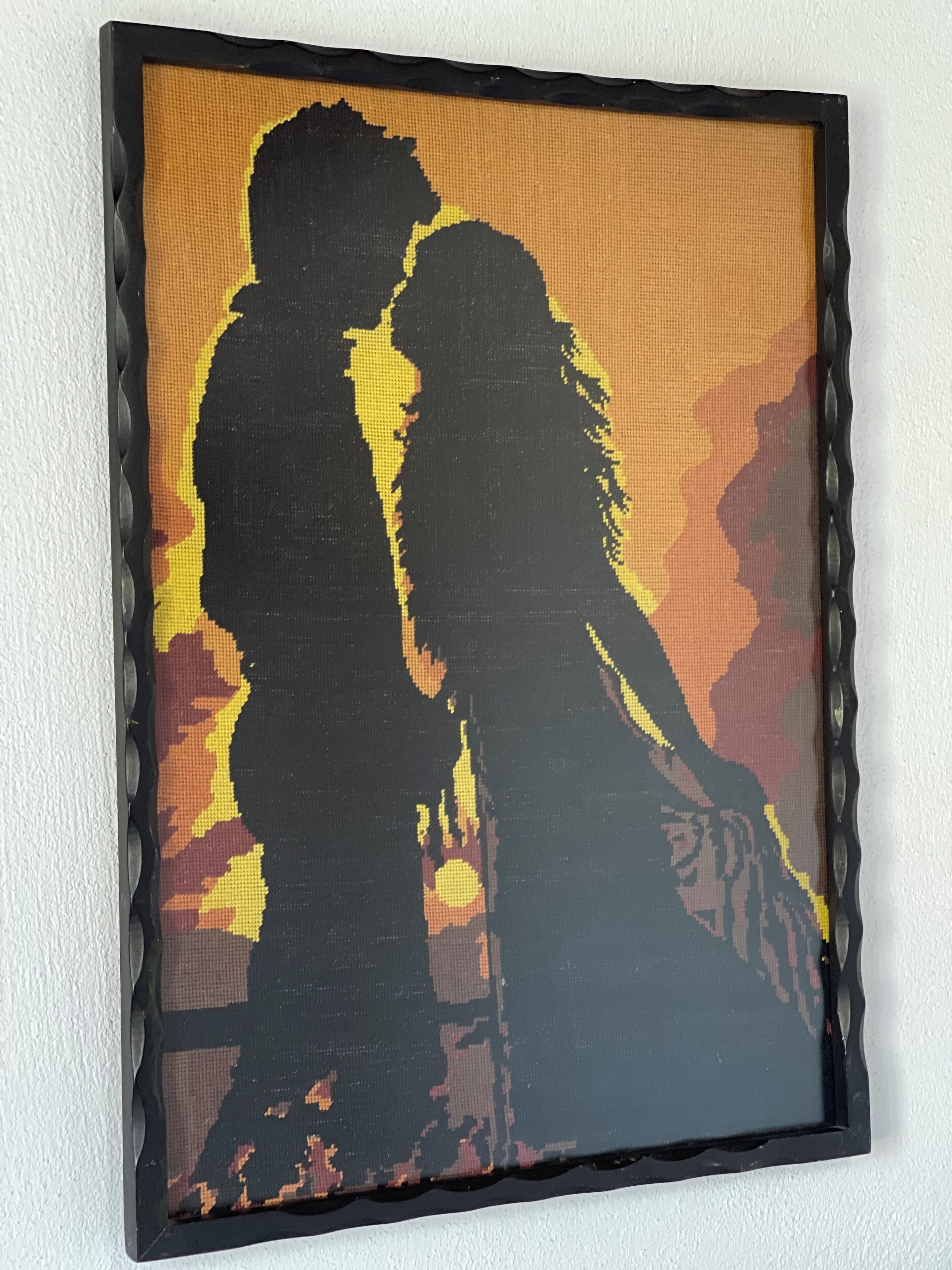 Obra de arte emoldurada retratando duas figuras em silhueta contra um céu ao pôr do sol.
