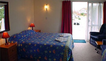 Quarto de hotel com cama, escrivaninha, cadeira, luminária e vista para o exterior.