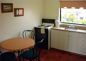 Uma cozinha compacta com fogão, pia e janela. Há uma mesa e duas cadeiras.