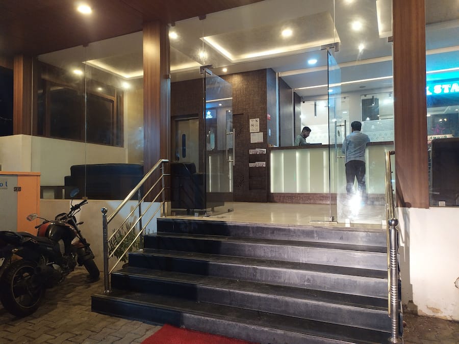 Um hall de hotel com balcão de recepção, escada que leva ao andar superior e uma motocicleta estacionada.