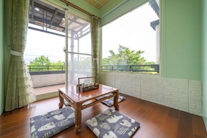Quarto com mesa de madeira, almofadas e vista para o verde lá fora.