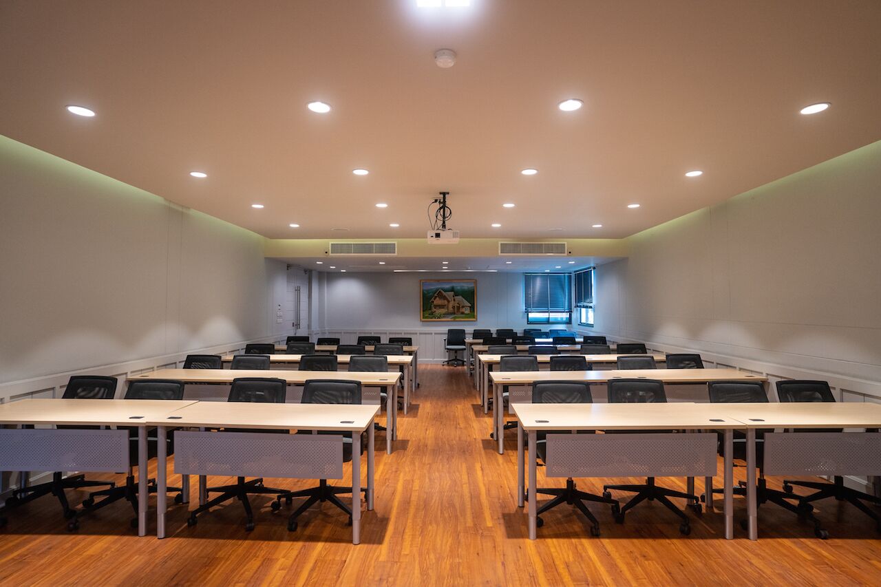 Uma sala de conferências com várias mesas e cadeiras, um projetor e um quadro na parede.