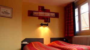 Quarto de hotel com duas camas, uma obra de arte na parede, abajur e janela com cortinas.