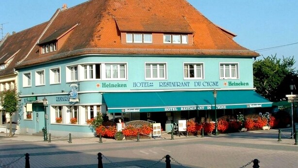 Hotel com fachada azul e toldo verde, exibindo o logotipo da Heineken.