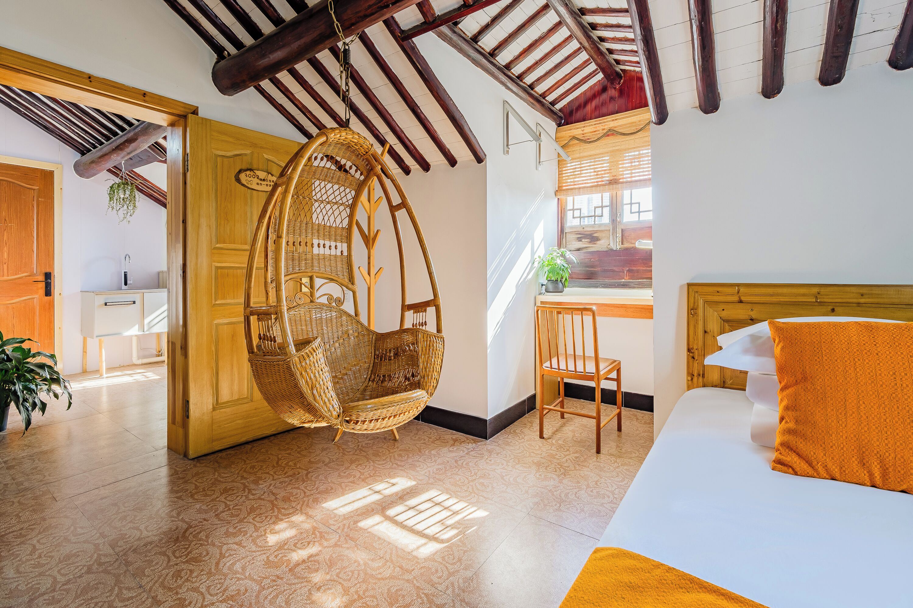 Quarto com cama, cadeira suspensa, porta de madeira e vista para o exterior.