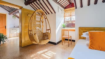 Quarto com cama, cadeira suspensa, porta de madeira e vista para o exterior.