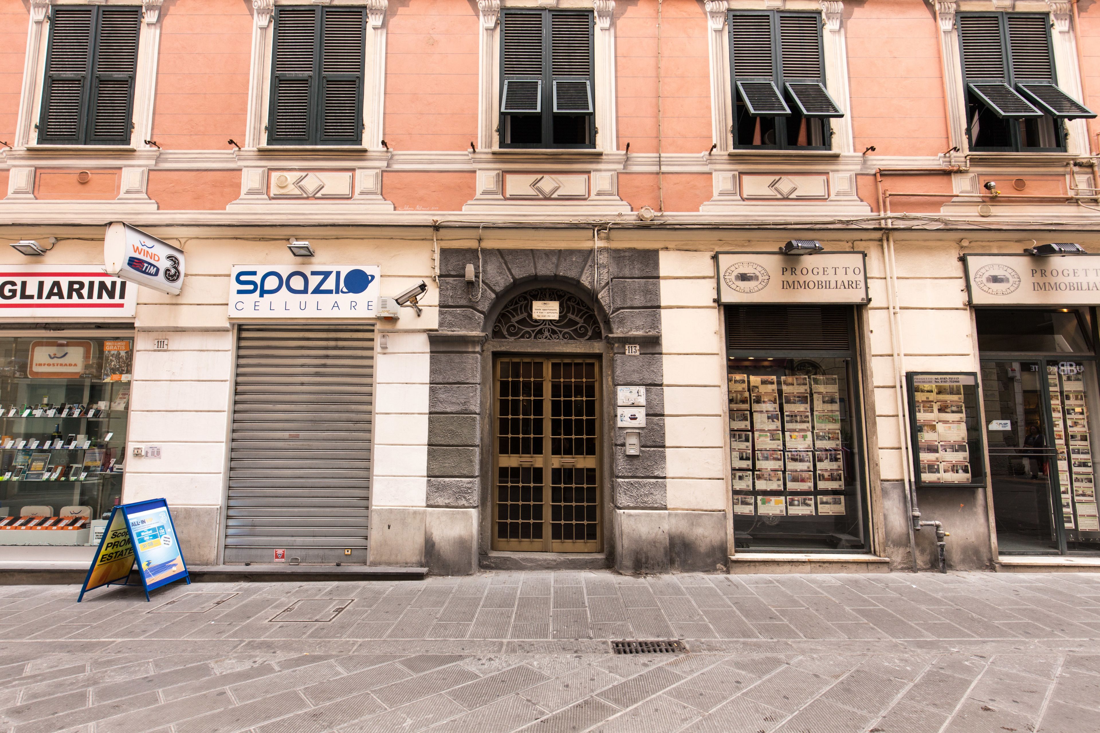 Fachada de edifício com uma loja fechada chamada "500ZI CELLULAR" e outra chamada "PROGETTO IMMOBILIARE".